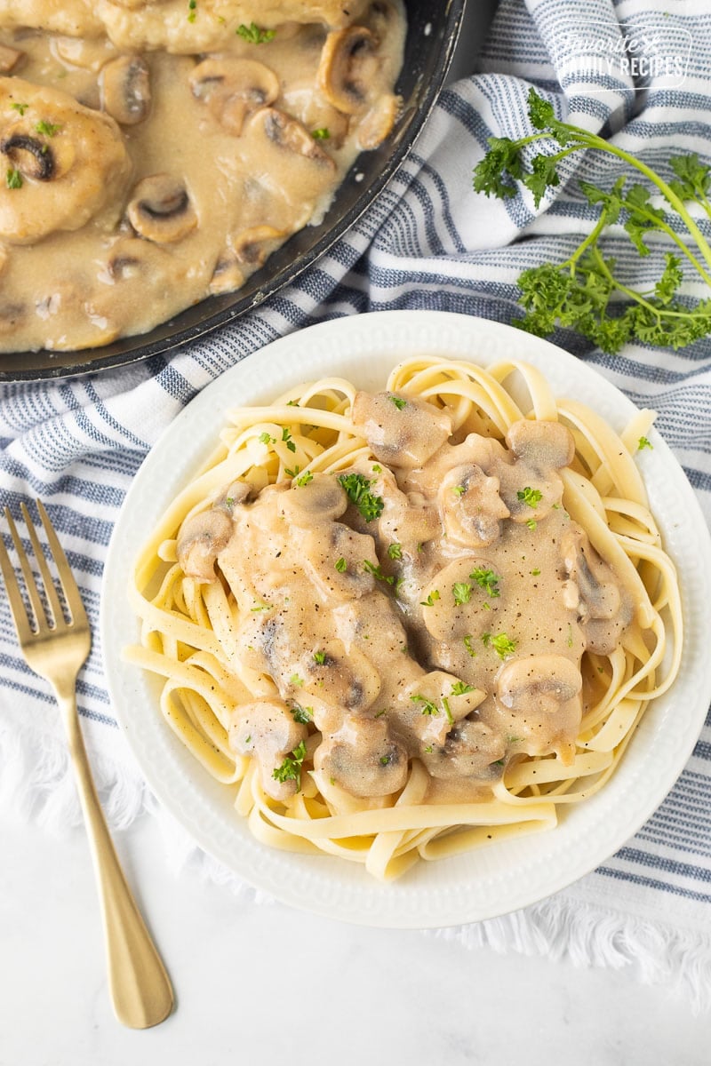 Plate of Chicken Marsala over pasta next to the skillet.